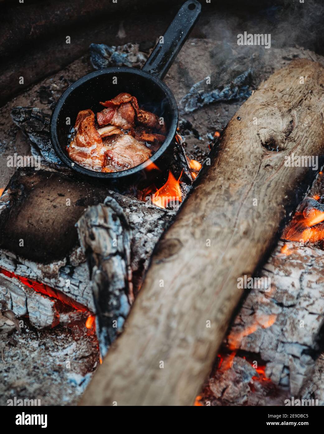 Top view closeup of bacon being cooked on the stove on a campfire while ...