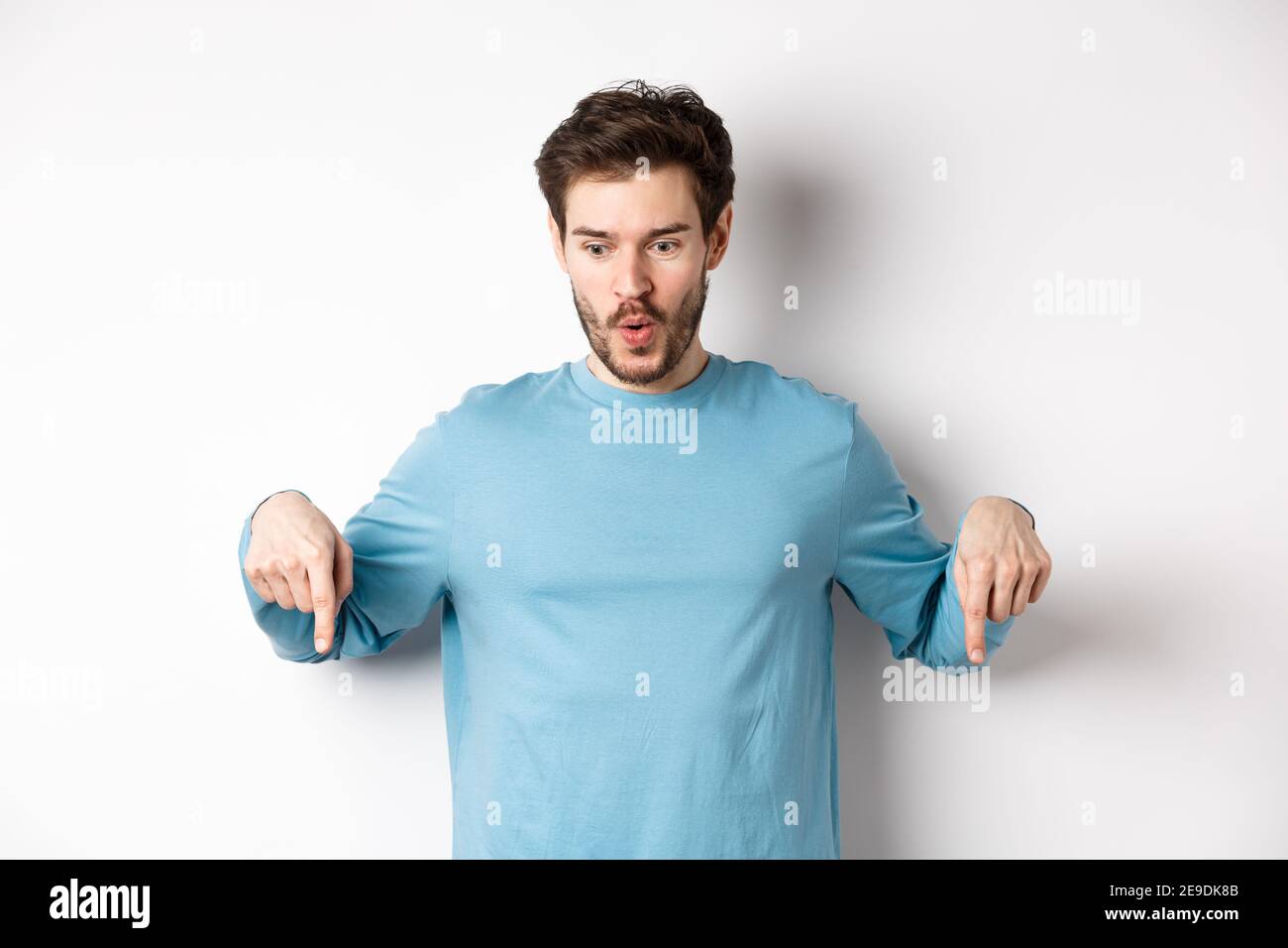 Handsome man pointing down with impressed and happy face, smiling and ...