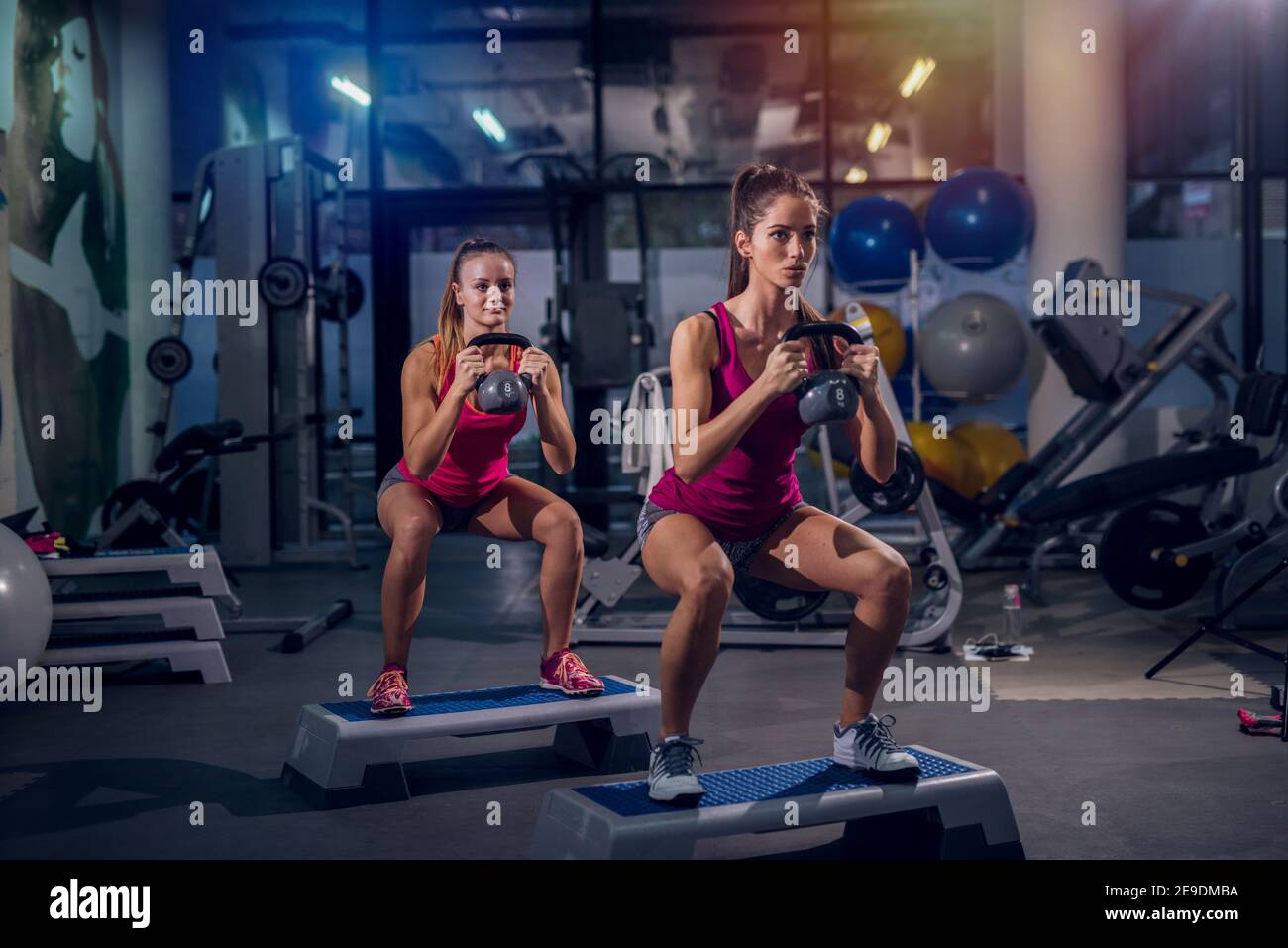 Two young fit girls working out in a gym. Standing on stepper and doing ...