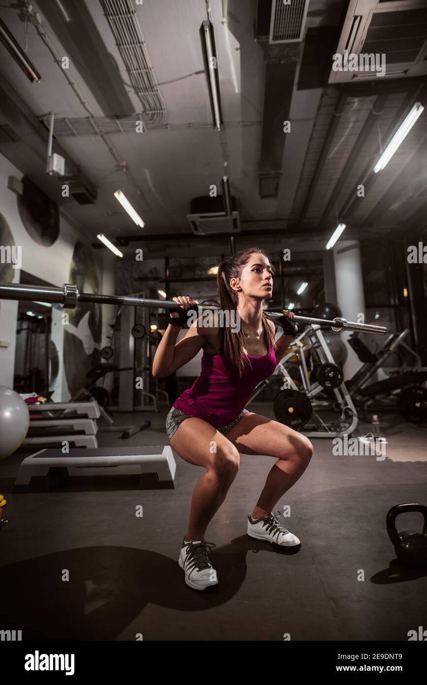 Strong woman in sportswear doing quats while holding weight bar on her ...