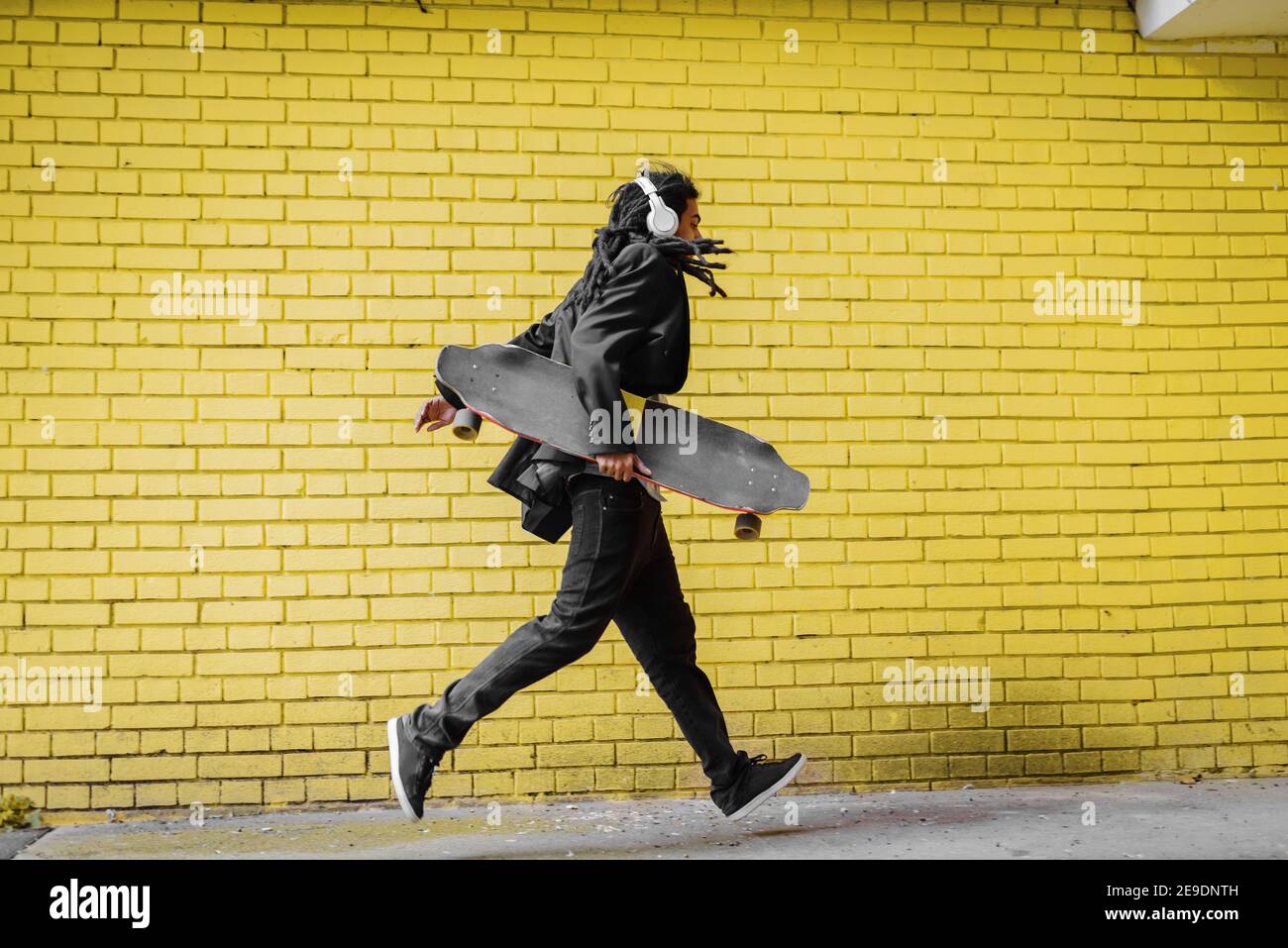 Modern urban young dreadlocks hipster man running with his skate in his ...