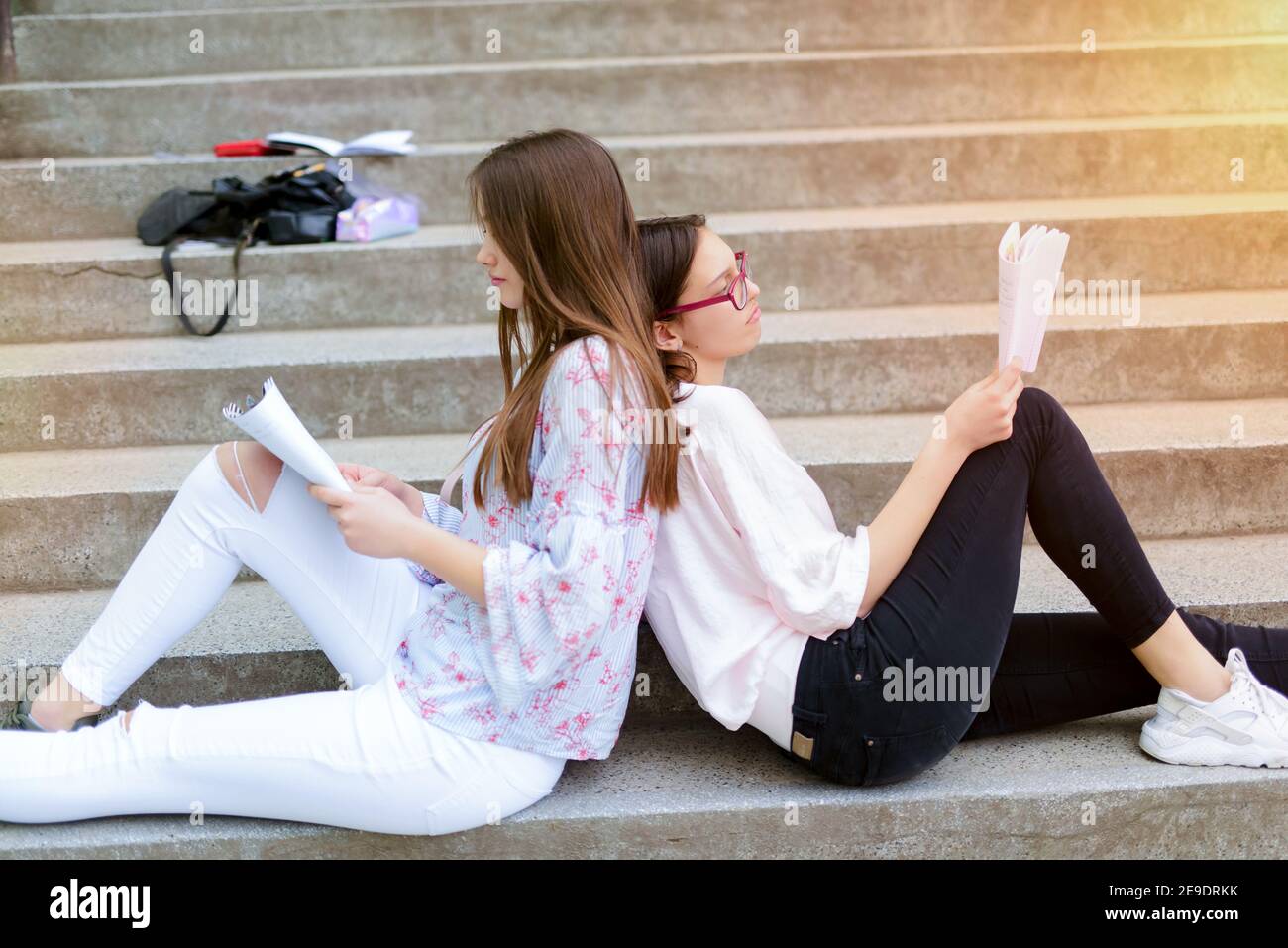 Two young school girls sitting on staircases in front of the school ...