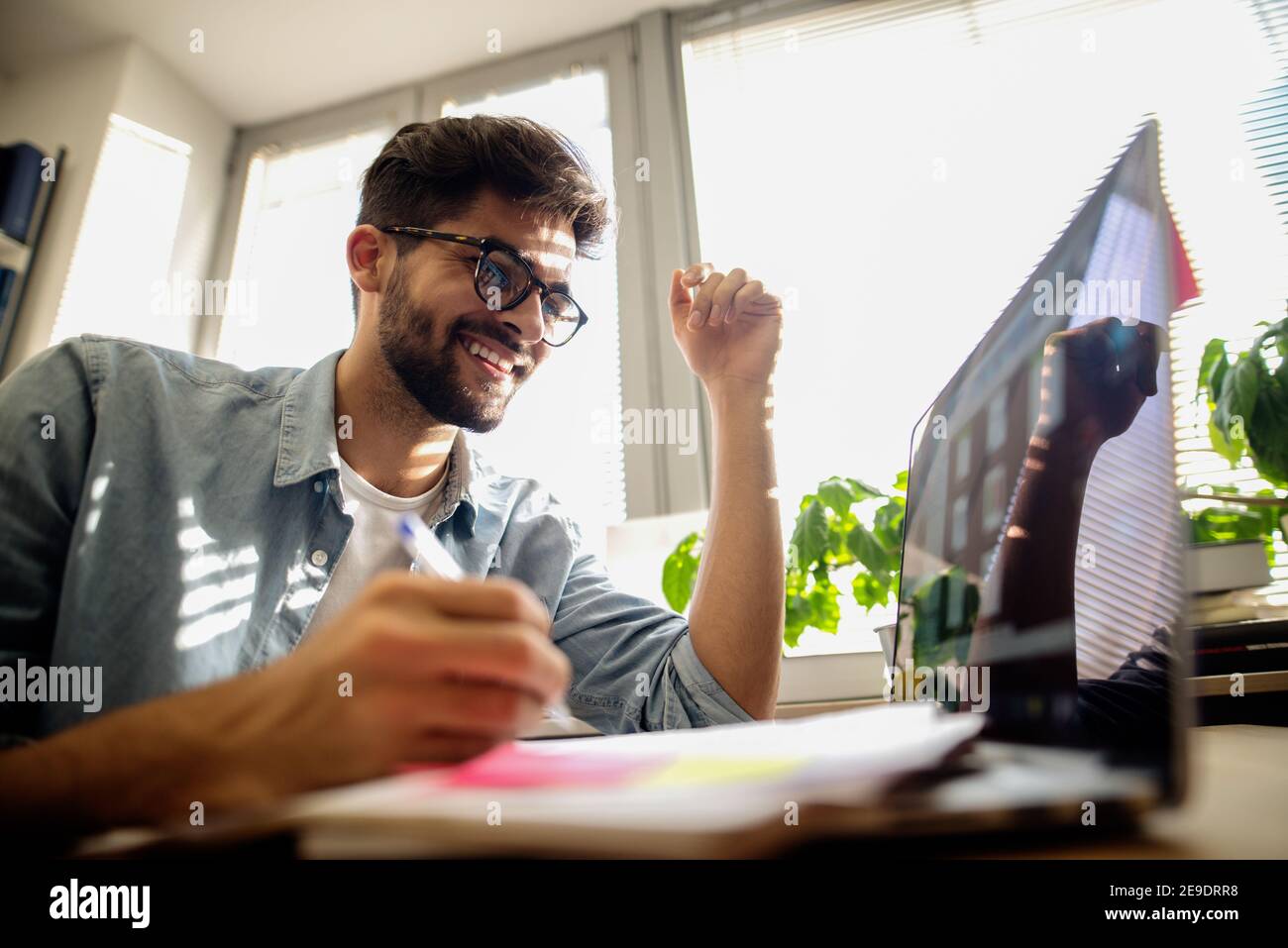 Happy male student learning for exam and using laptop while studying in ...