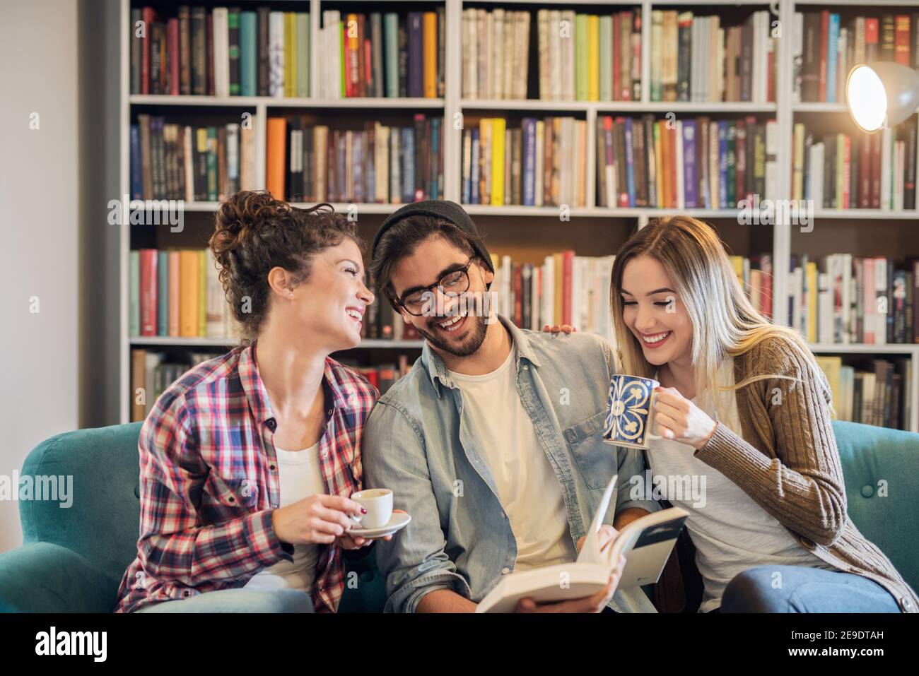 Happy students sitting on sofa and discussing book. In background ...