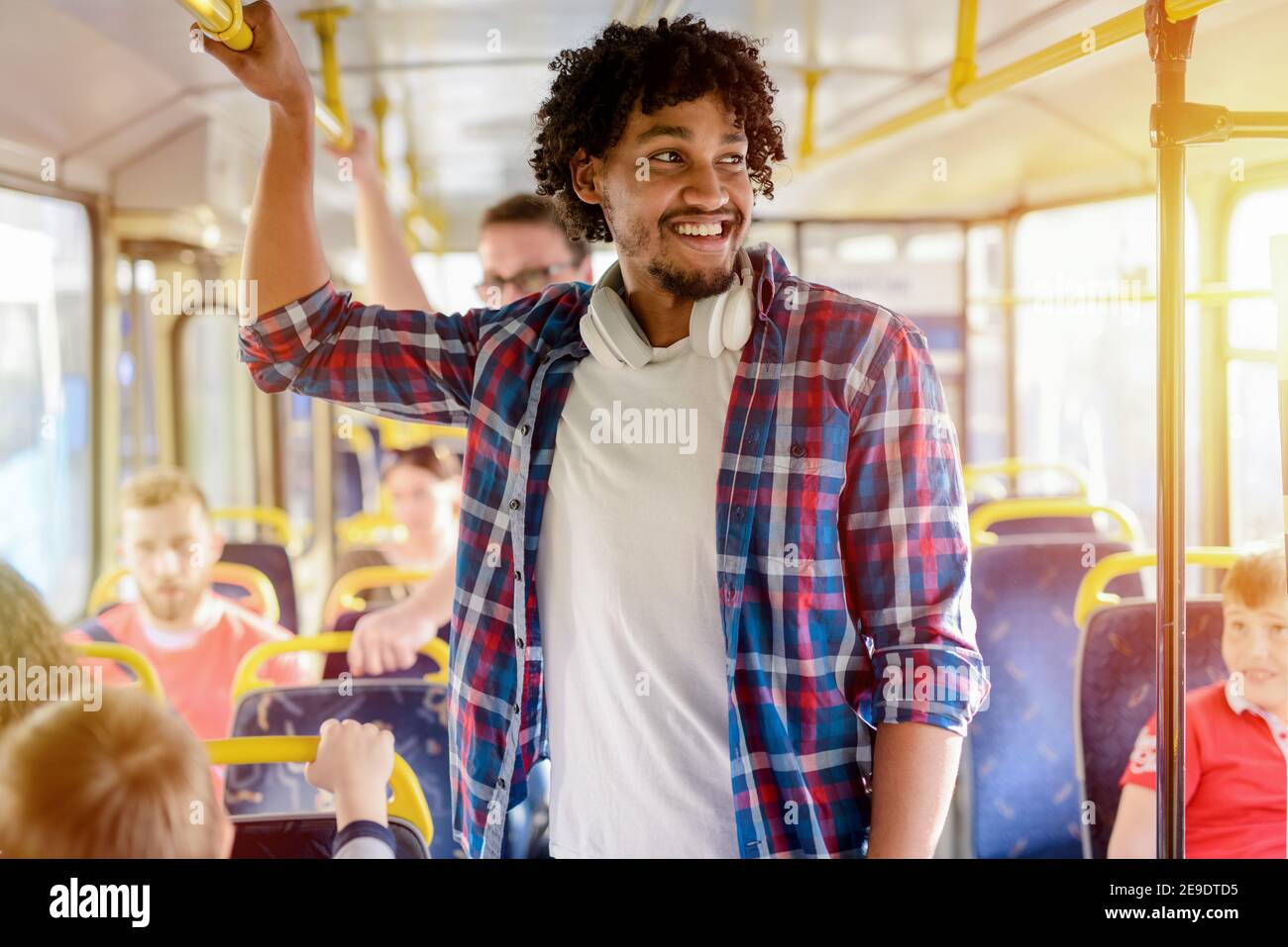 Young happy Afro.American holding for a bar in a bus with headphones ...