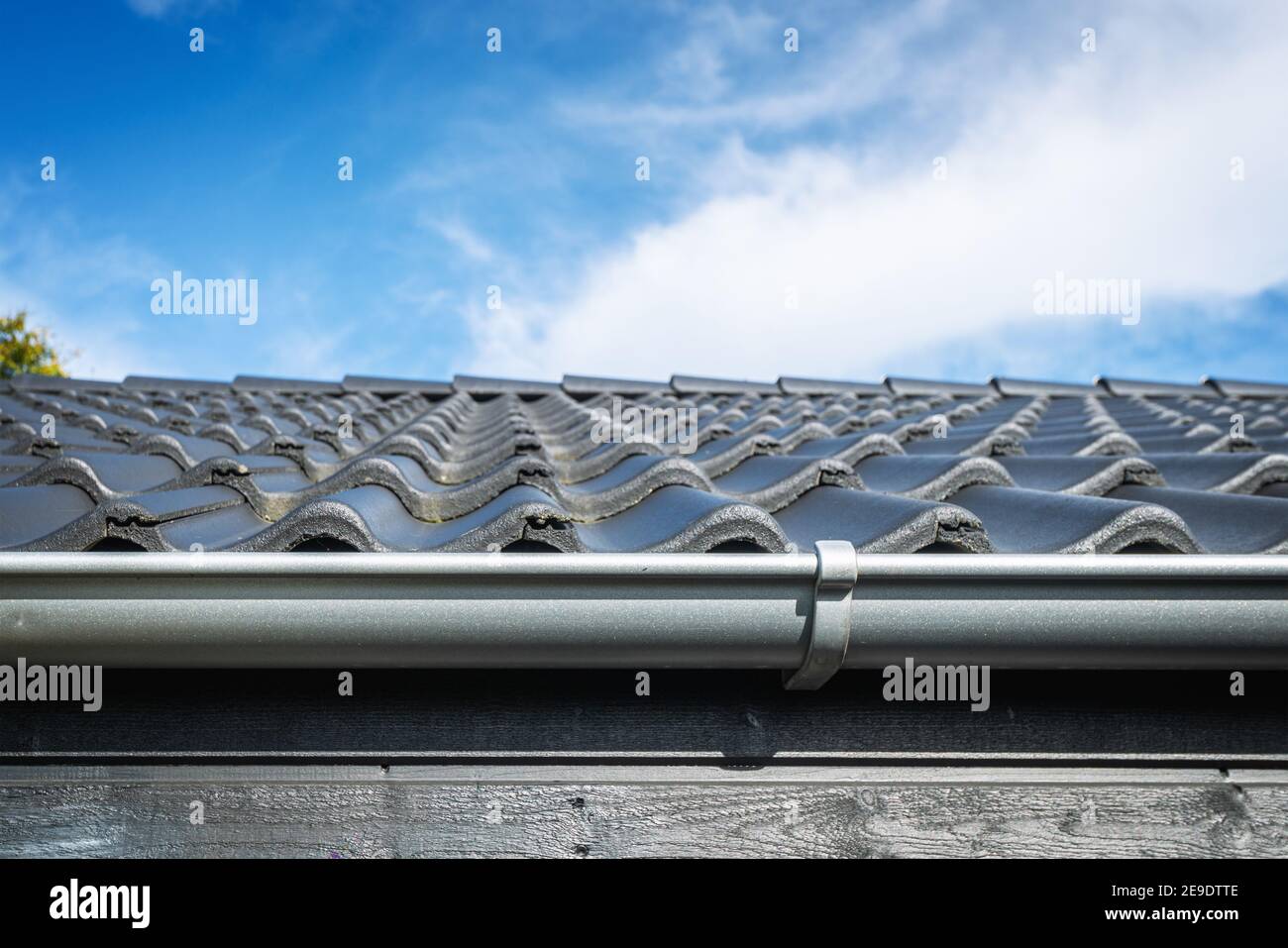 Roof on a house with tiles and a gutter. Clean rooftop under a blue sky ...