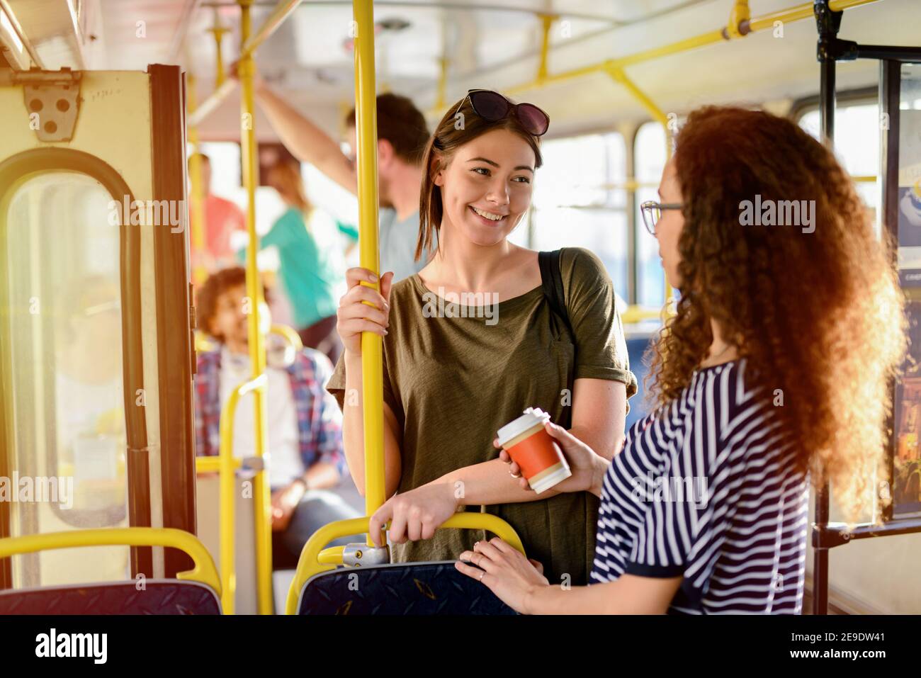Two girlfriends standing in a bus and talking. Traveling together to ...