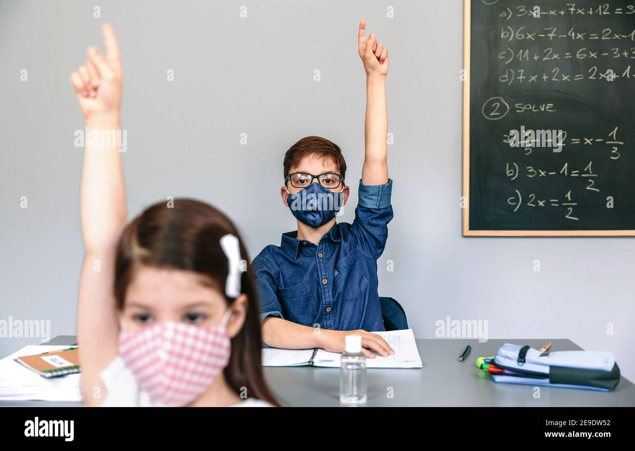 Students with masks raising hands at school Stock Photo - Alamy