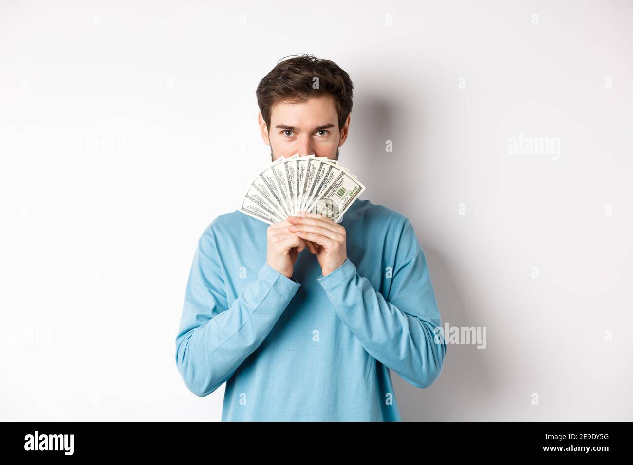 Finance concept. Smiling young man covering face behind money, showing ...