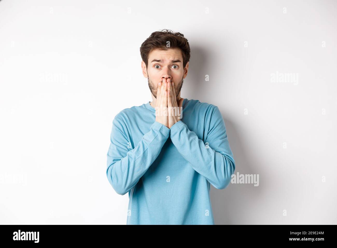 Shocked and worried young man gasping and covering mouth, look with ...