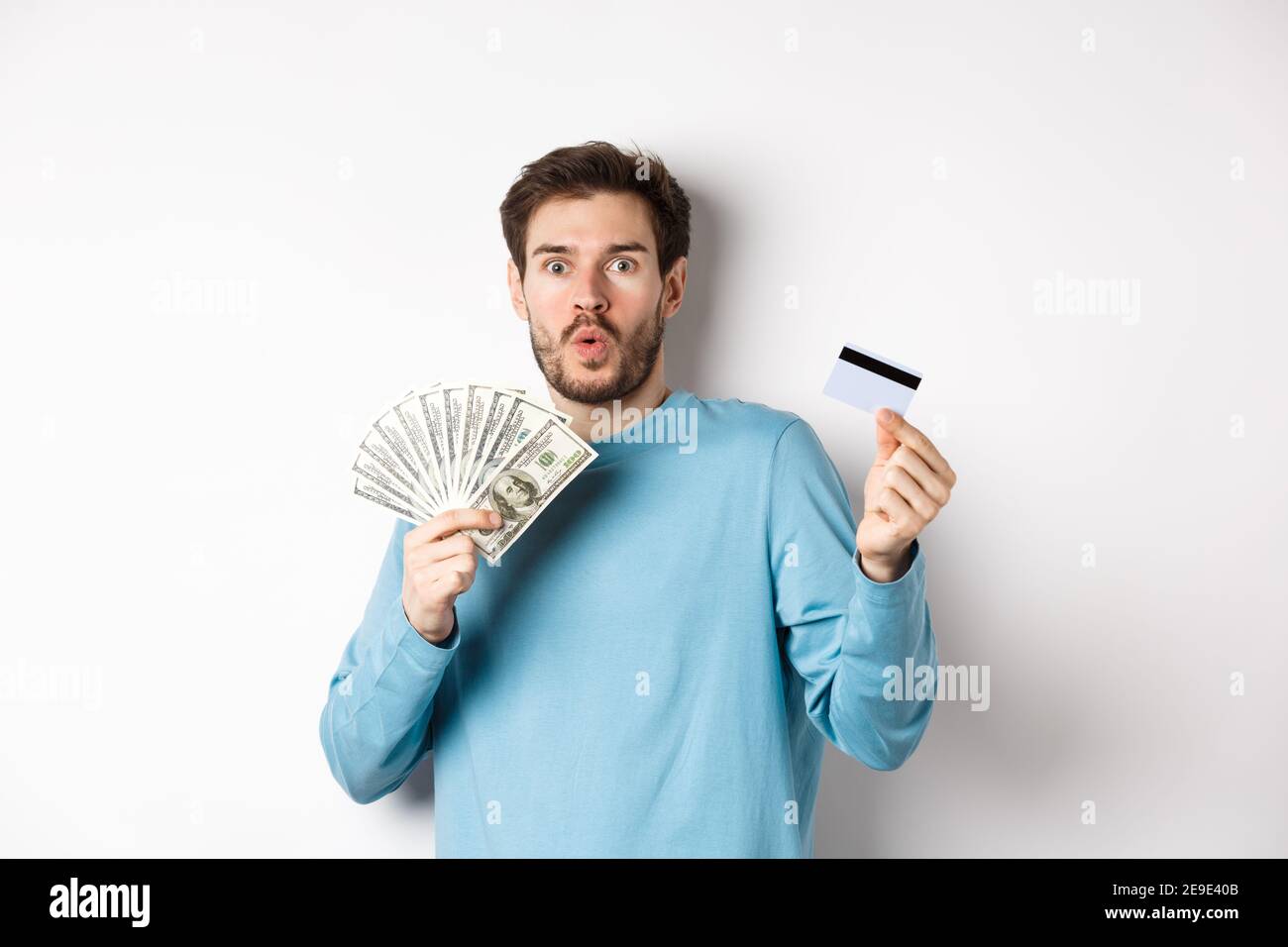 Surprised young man showing money in dollars and plastic credit card ...