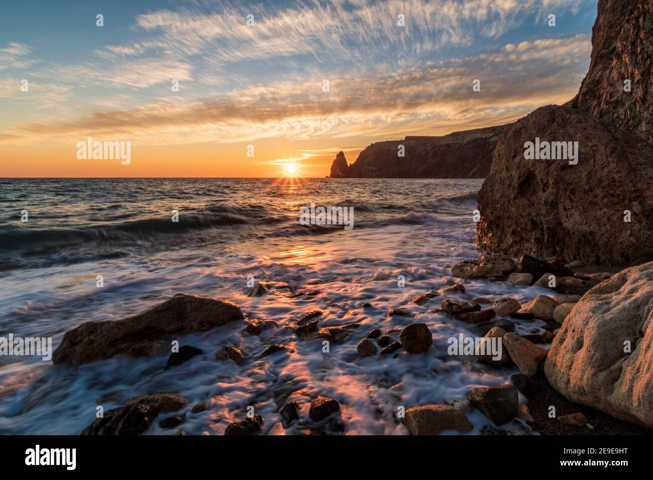 Bright sea sunset. The waves crash into the rock, lit by the warm ...