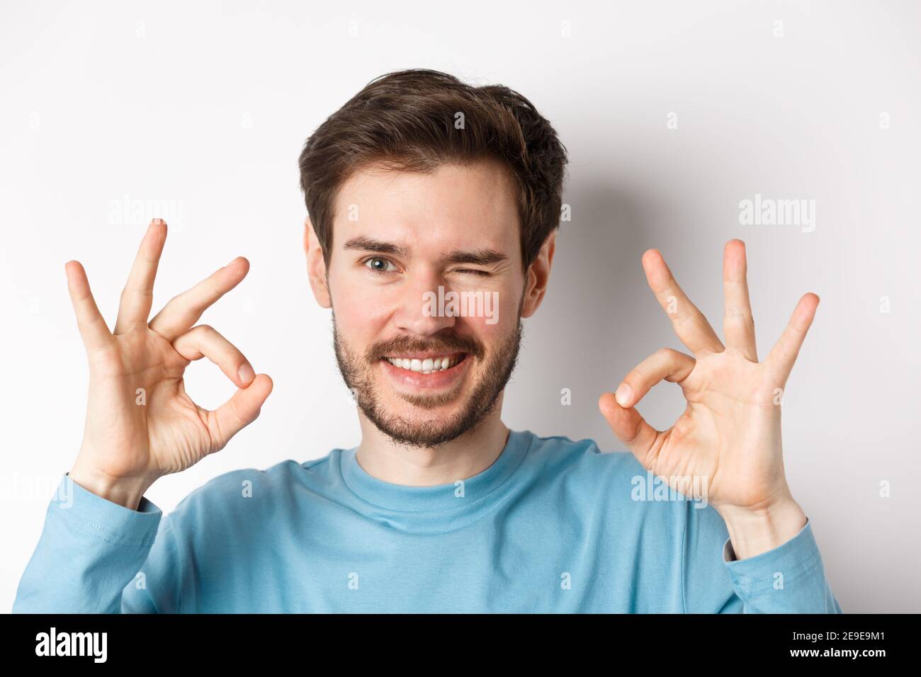 Close up of handsome bearded man winking and smiling, showing okay ...