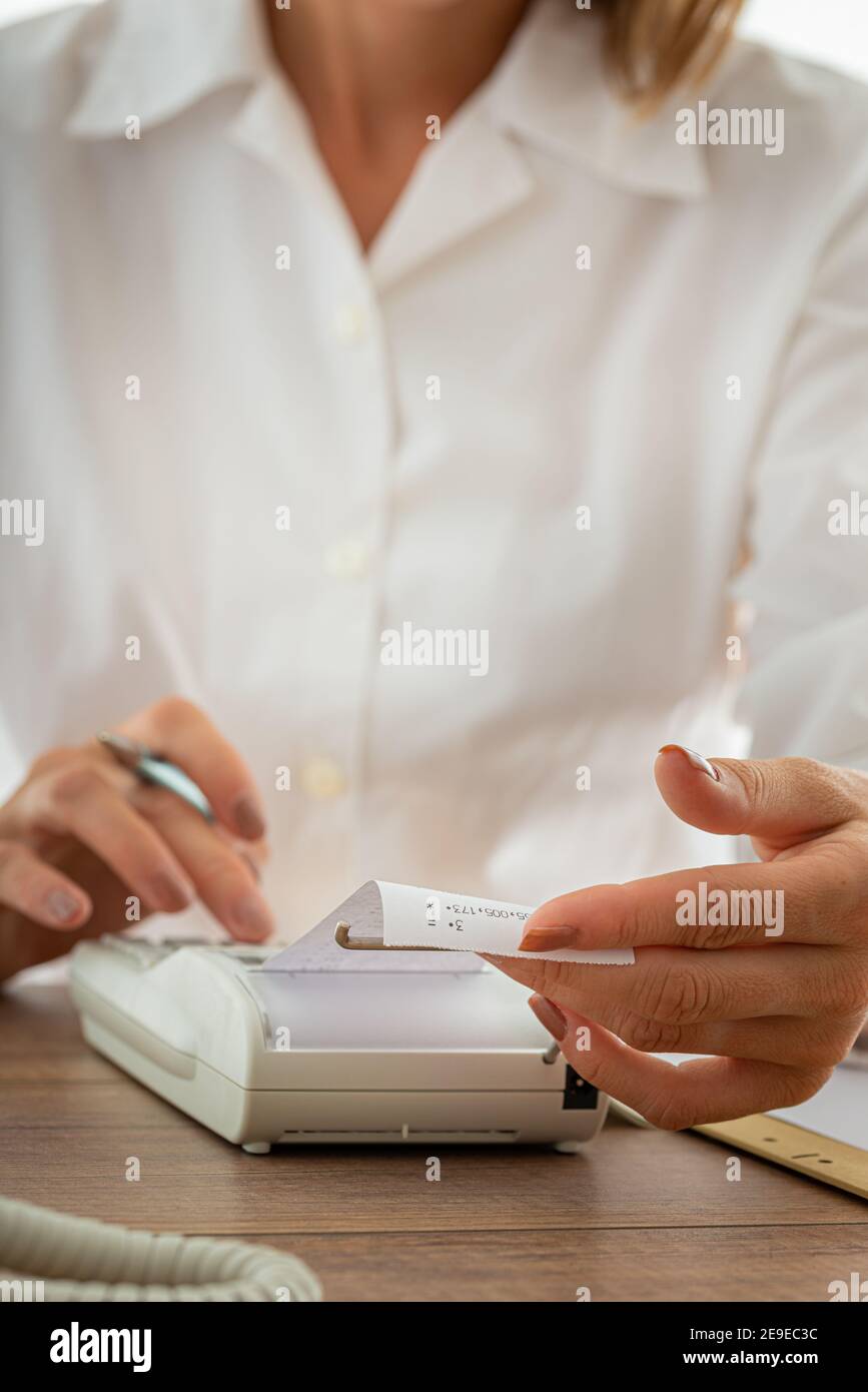 Female accountant using adding machine while working on company ...