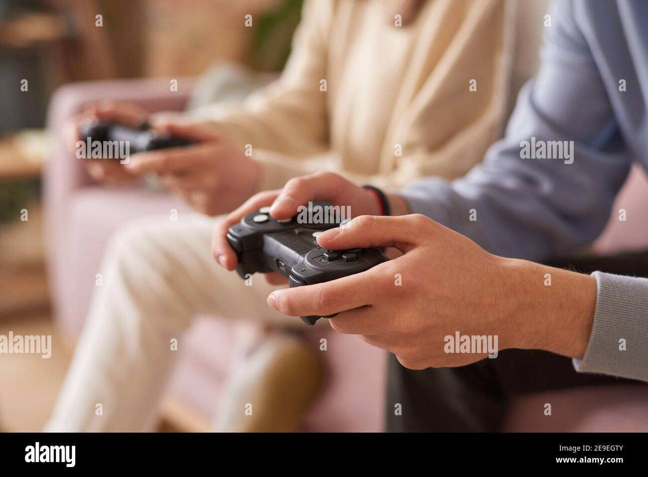 Close-up of people sitting on sofa with joysticks and playing video ...