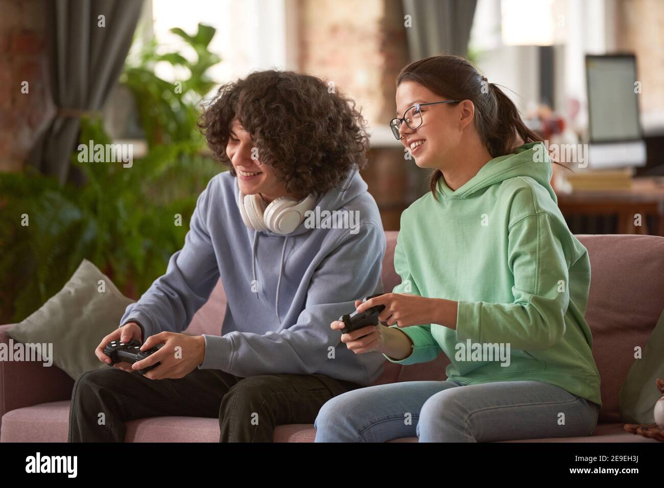 Two friends sitting on sofa using joysticks to play video games in team ...