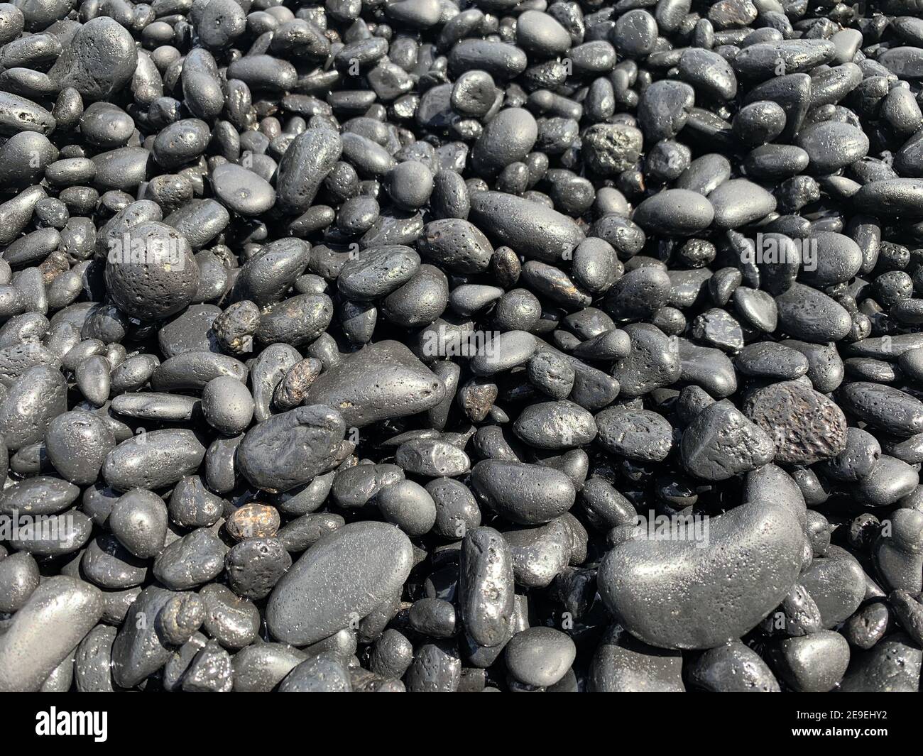 Of black volcanic rounded rocks smoothed by the ocean at beach on the ...