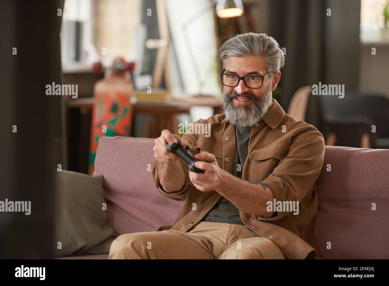 Mature bearded gamer looking exciting playing video game on sofa in the ...