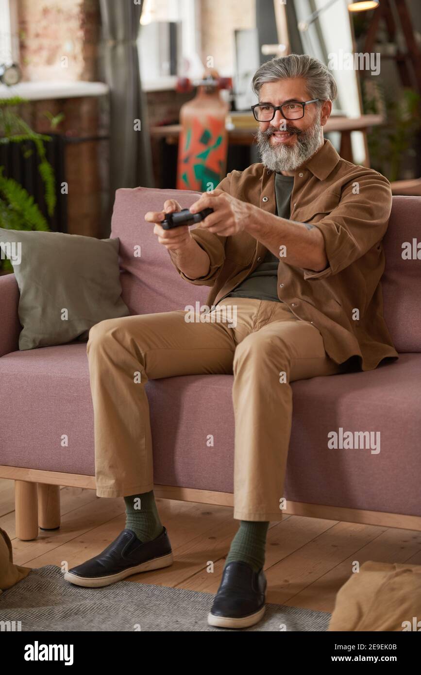 Mature gamer using joystick to play video game on TV while sitting on ...