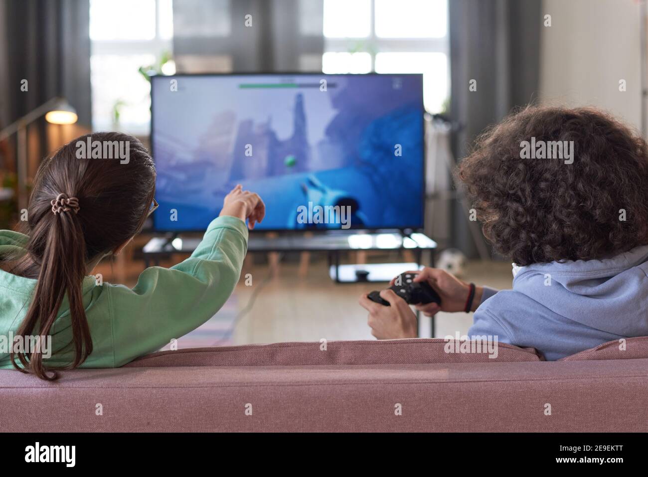 Rear view of two friends sitting on sofa and playing video game ...