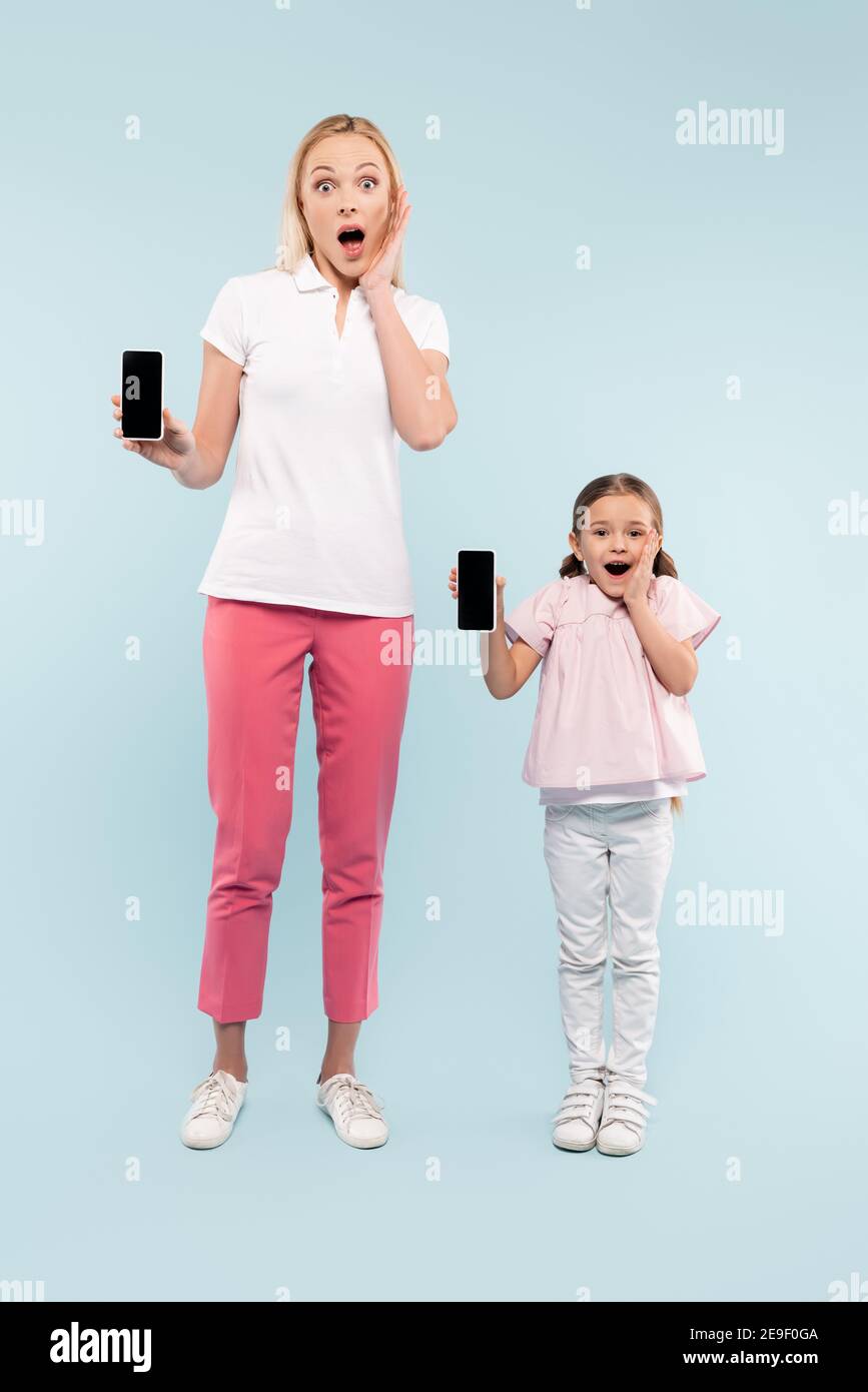 full length of shocked mother and daughter holding smartphones with ...