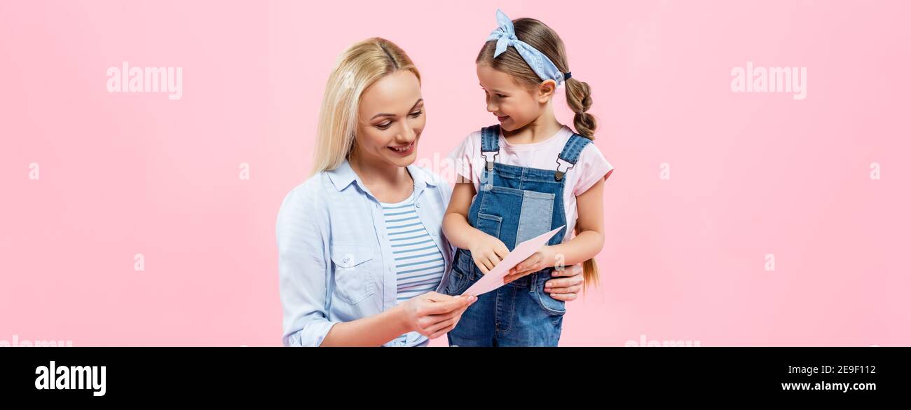 happy child holding greeting card near mother isolated on pink, banner ...