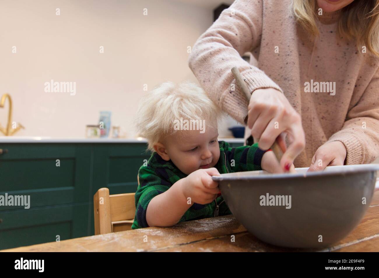Mother and child mixing ingredients in a bowl in the kitchen together ...