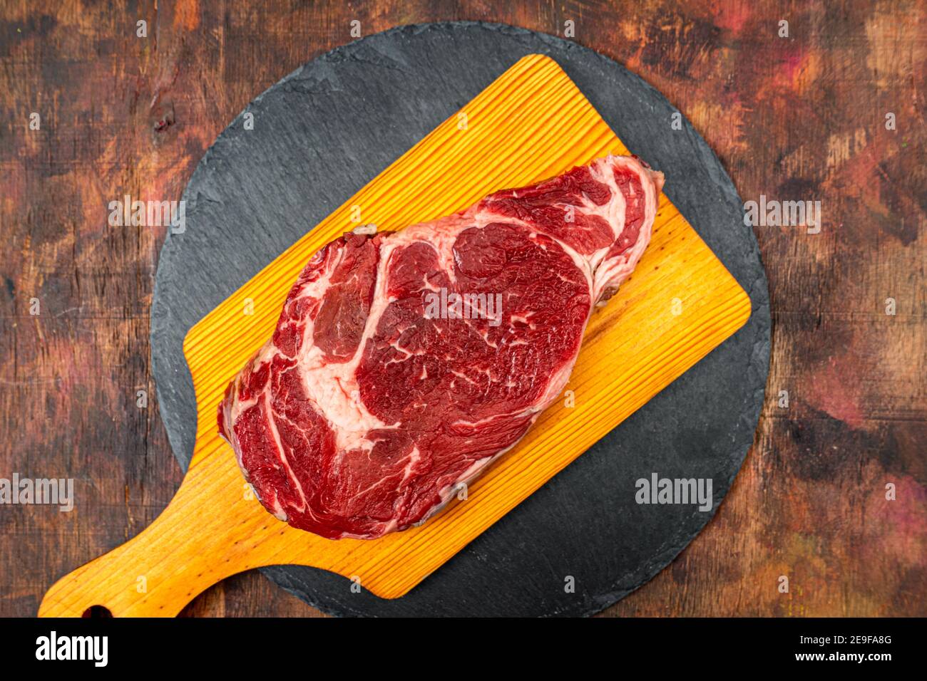 Raw beef ribeye on a round slate plate on an old wooden table in brown ...