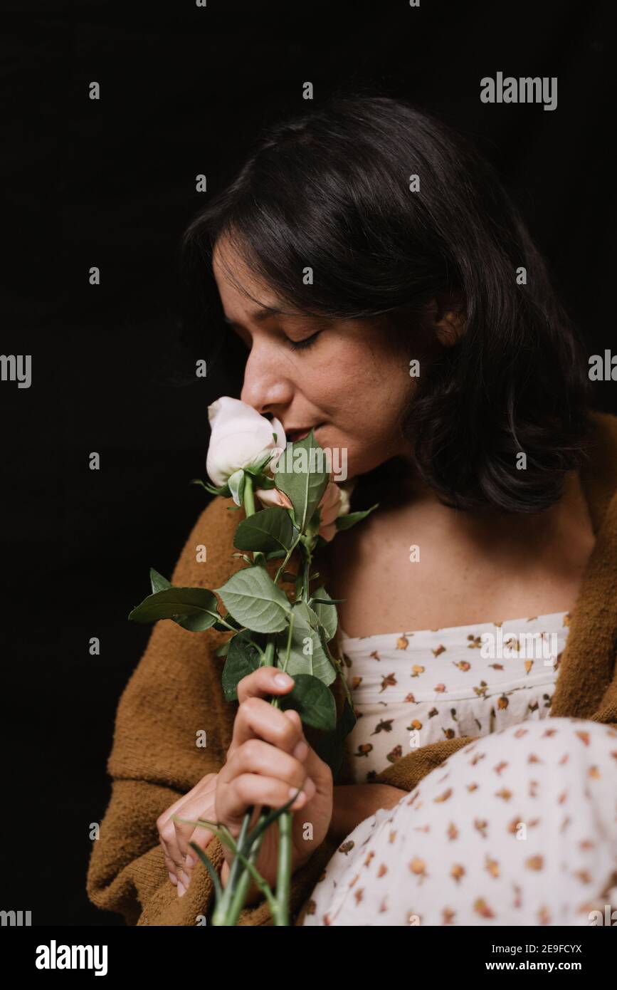 young woman smelling white rose on black background portrait. closed ...