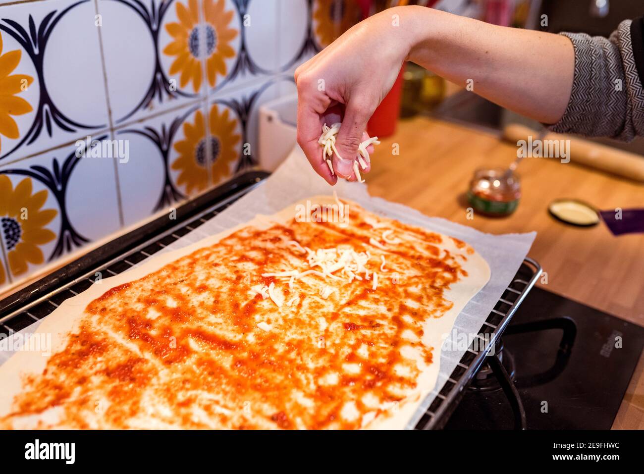 Hand sprinkling grated cheese over the tomato and a dough. Preparing a ...