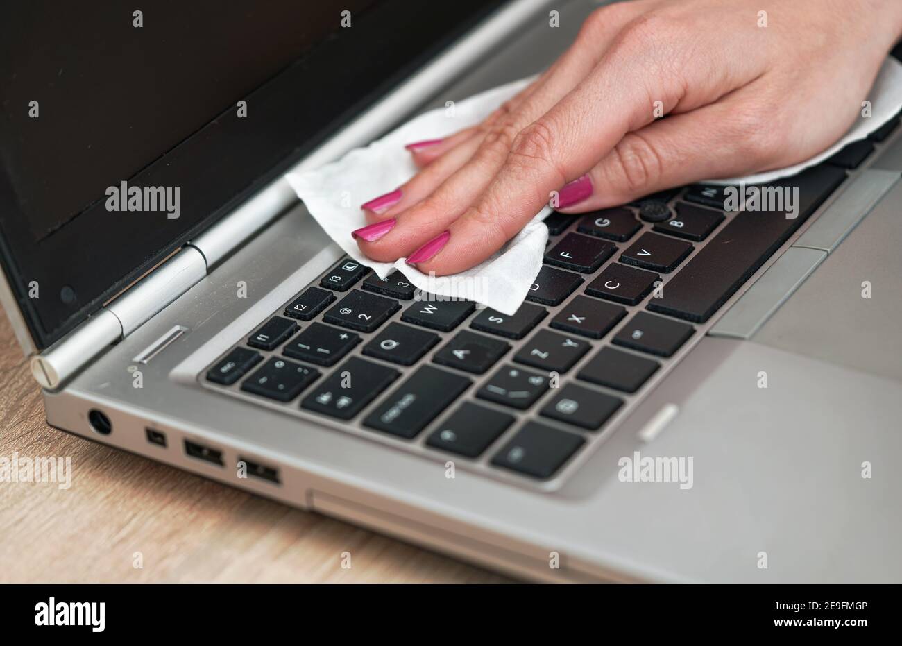 Woman cleaning laptop keyboard with white tissue, detail on her fingers ...