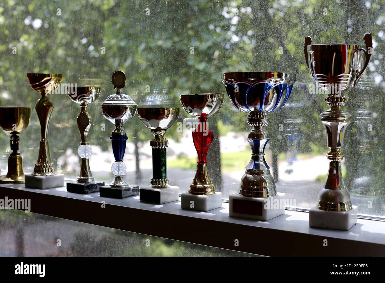 Group of sport trophies in row in a sport hall against windows as green ...