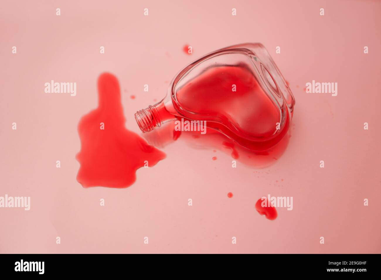 Heart shaped transparent bottle tilted on a pink surface with red ...