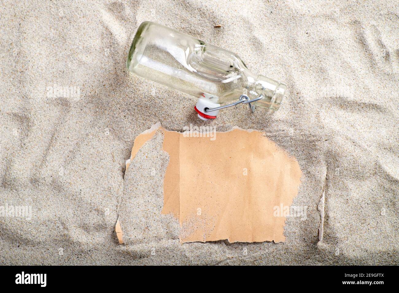 Gray blank paper covered with sand and a glass open bottle in the sand ...