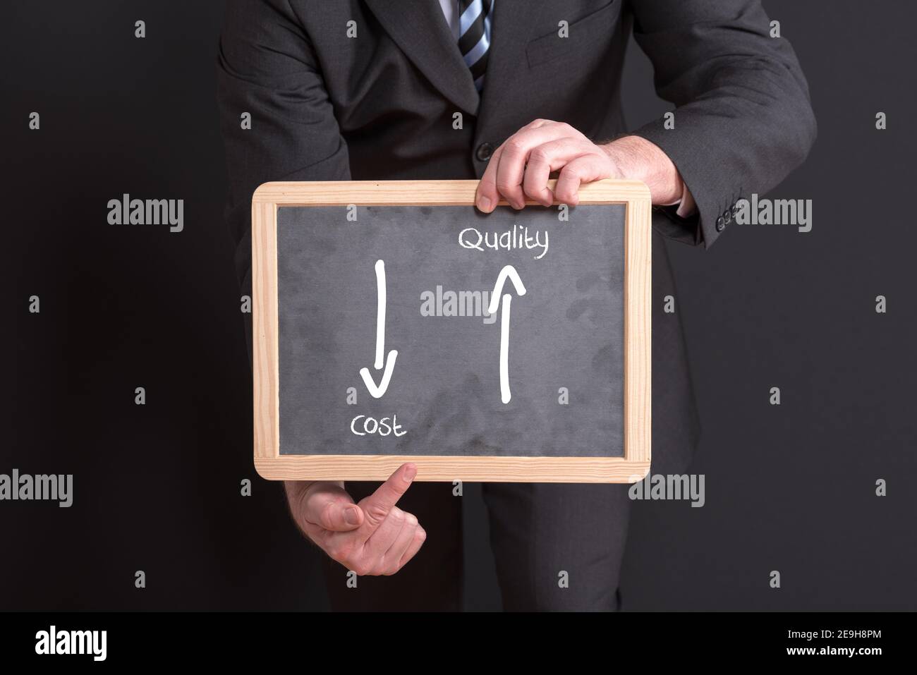 Businessman holding a chalkboard with two arrows with cost and quality ...