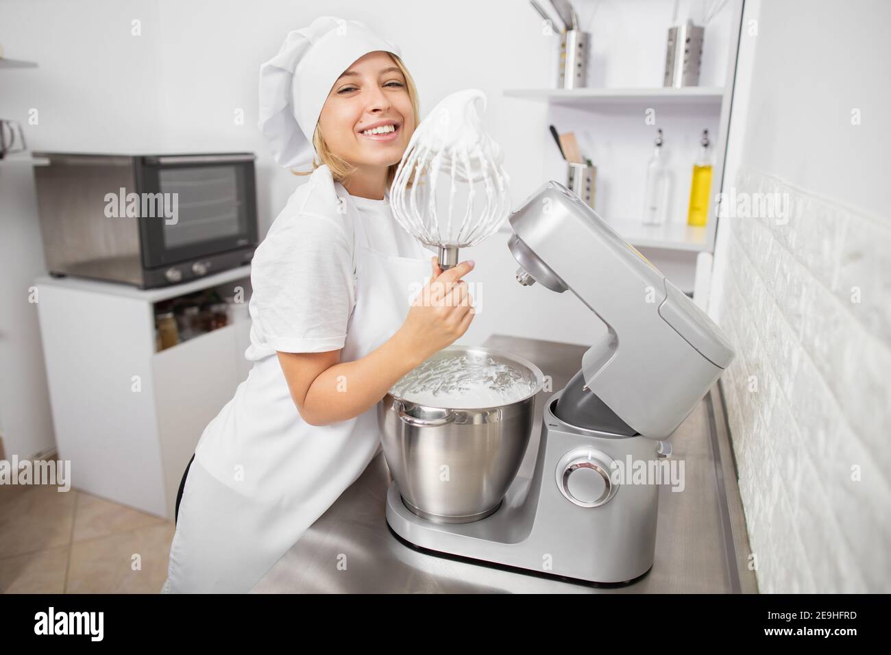 Happy pretty confectioner girl holding an electric whisk with whipping ...