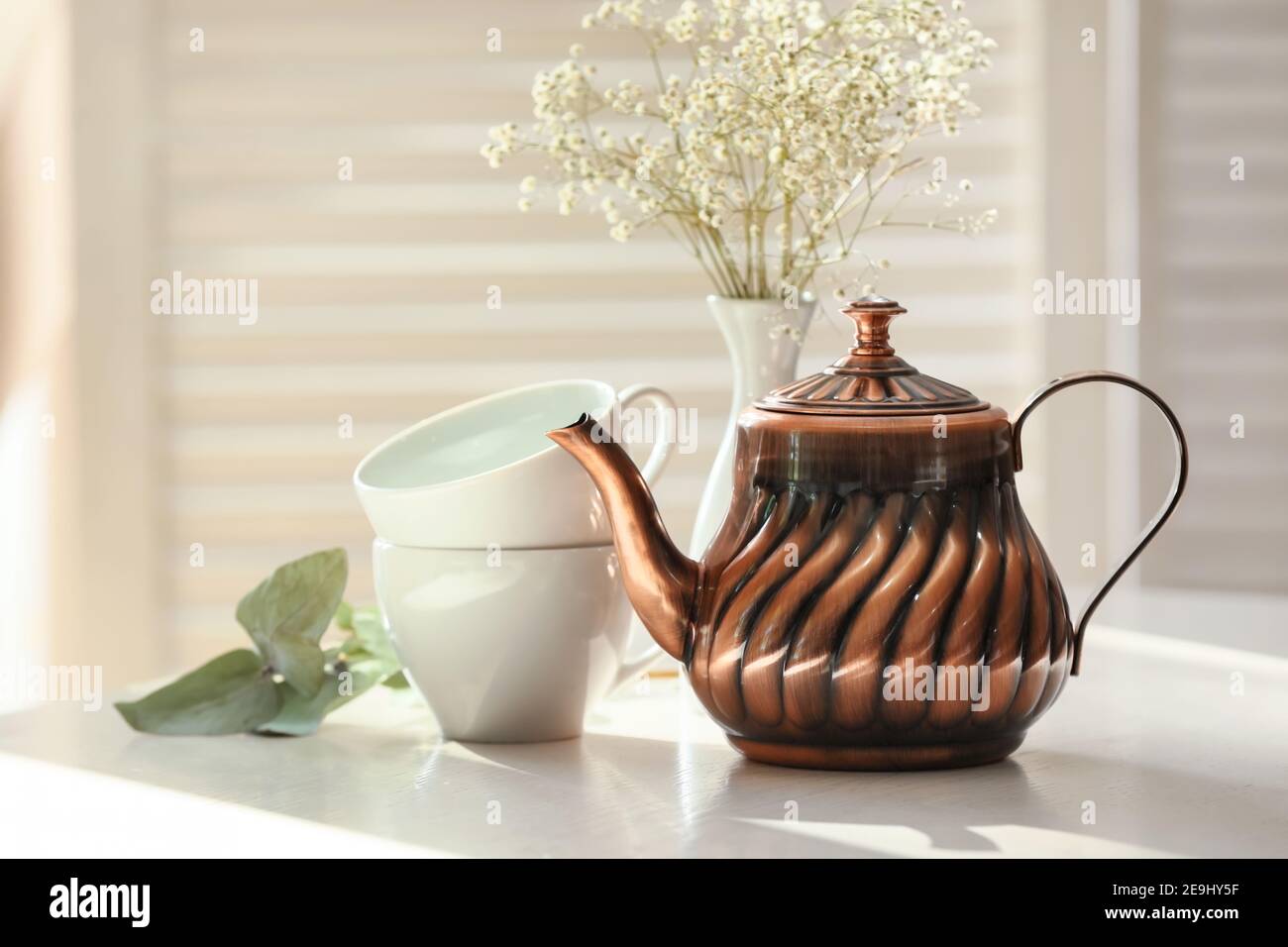 Stylish teapot and cups on light table in room Stock Photo - Alamy
