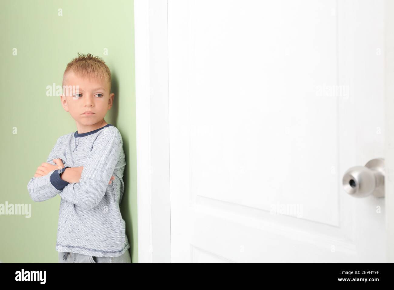 Sad little boy near closed door in room Stock Photo - Alamy