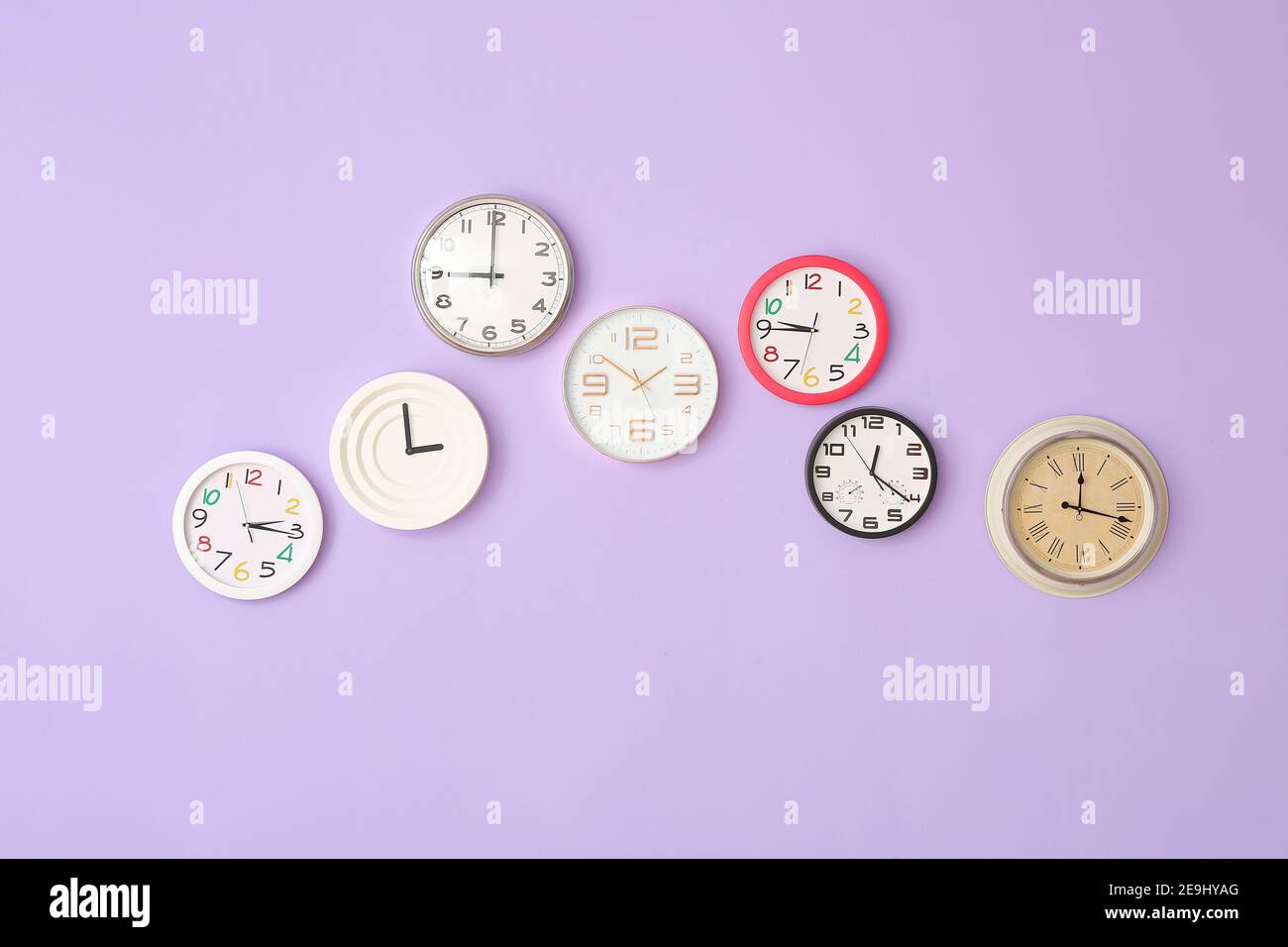 Different clocks hanging on color wall Stock Photo - Alamy
