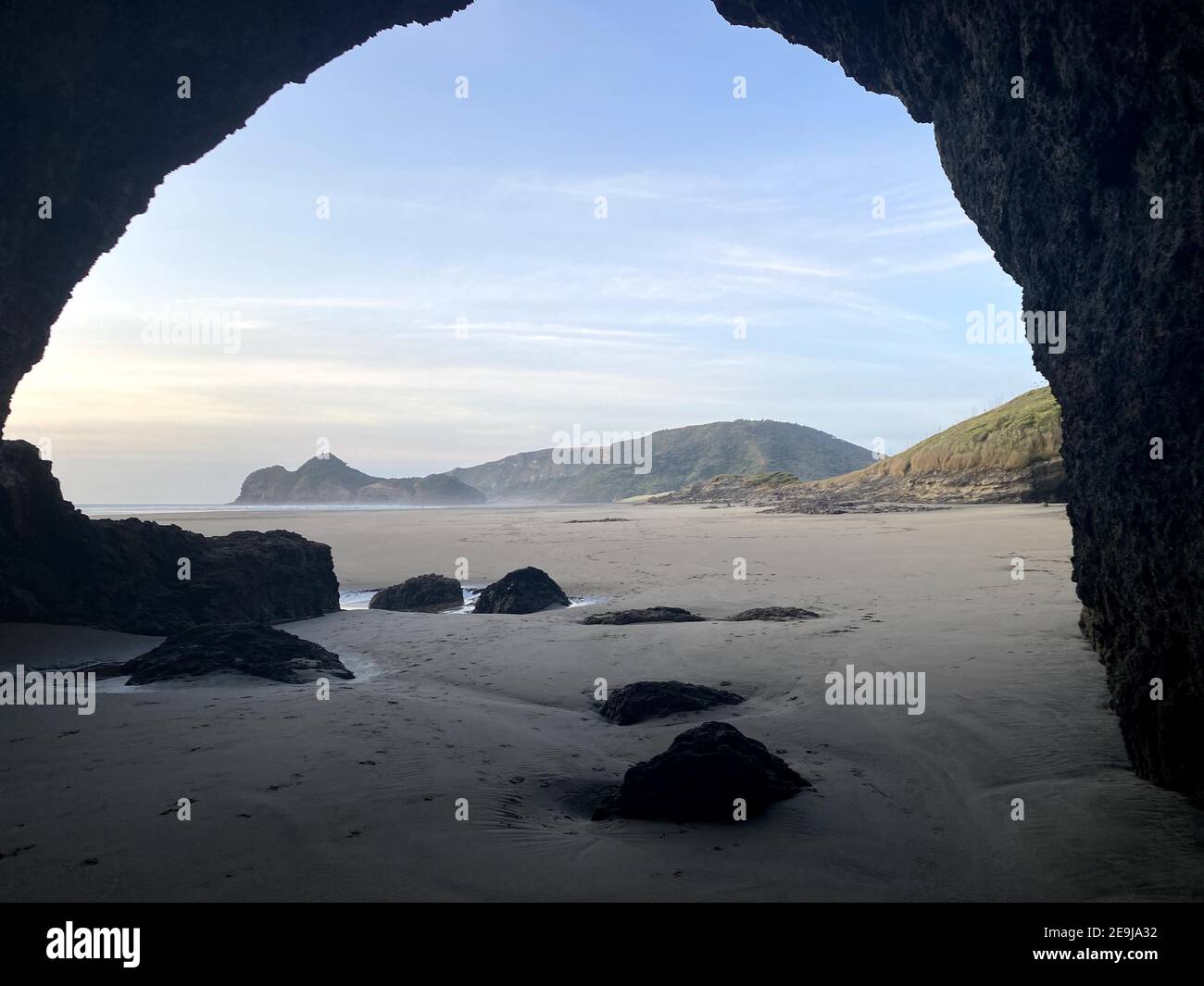 Mesmerizing view of the sandy beach surrounded by cliffs from a cave ...