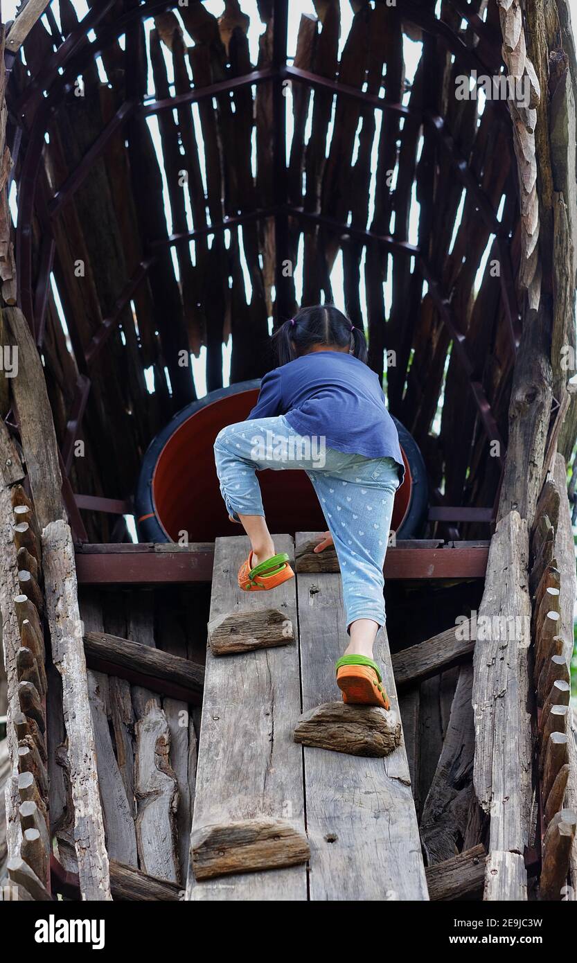 The back view of a young girl climbing up a wooden steep ramp at a park ...