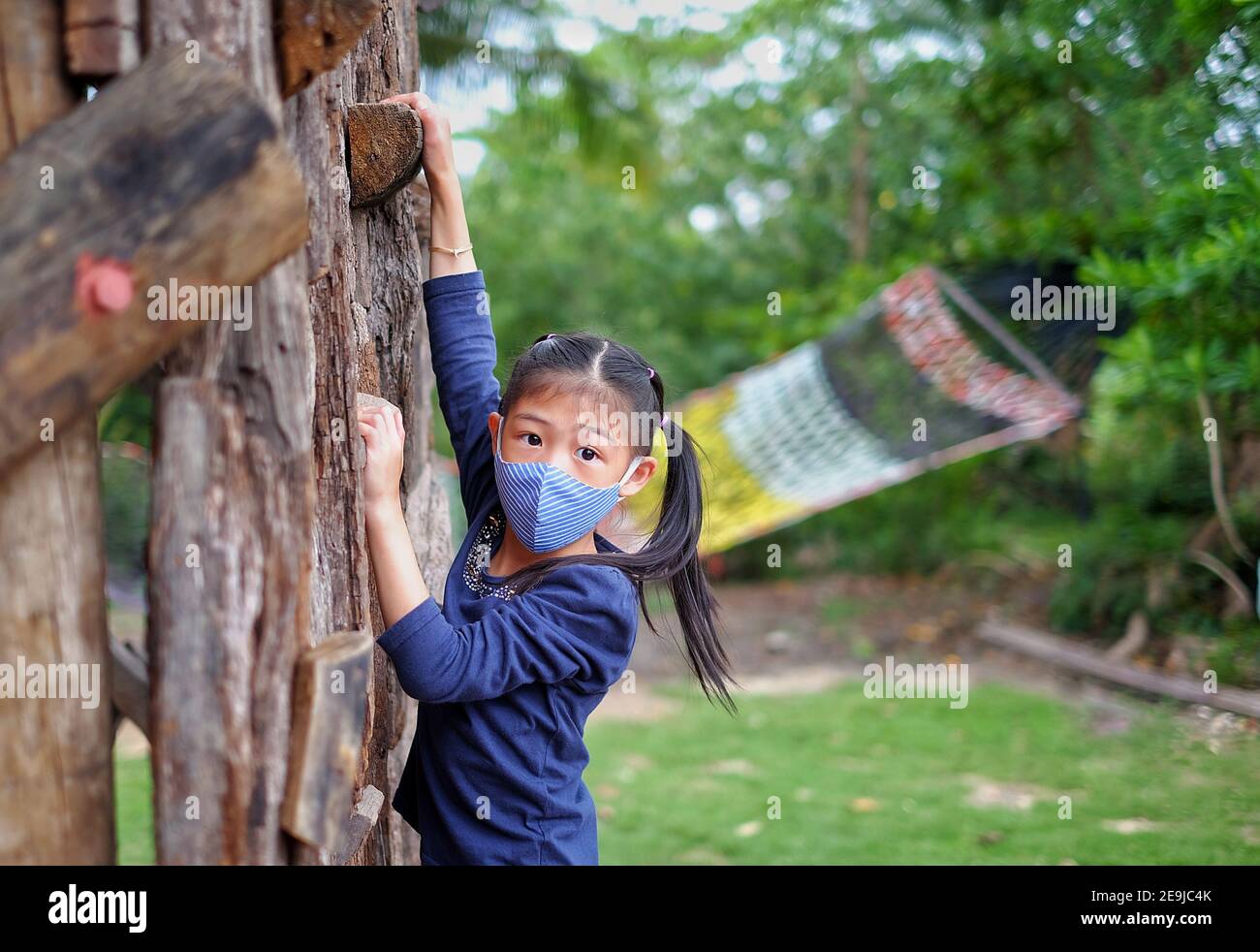A cute young Asian girl with a face mask is climbing a wall of an ...