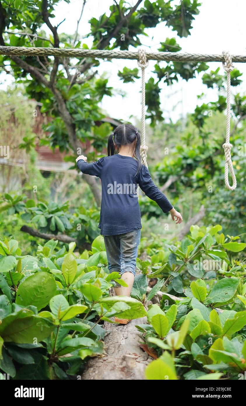The back view of a cute young Asian girl trying to walk across a small ...