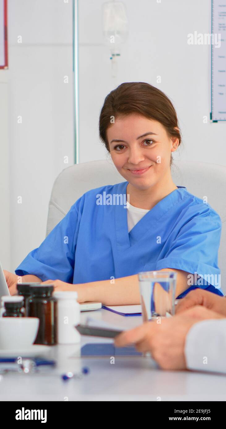 Nurse writing on laptop during conference and looking at camera smiling ...