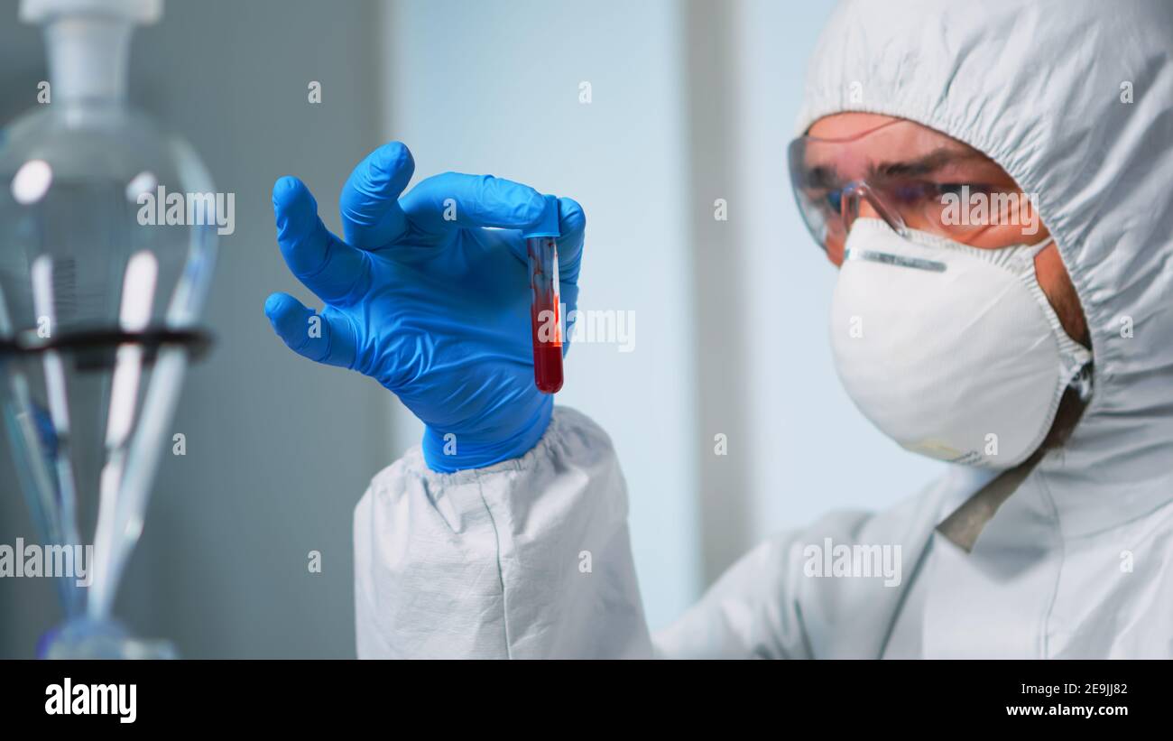 Scientist holding blood sample wearing protection suit analysing virus ...