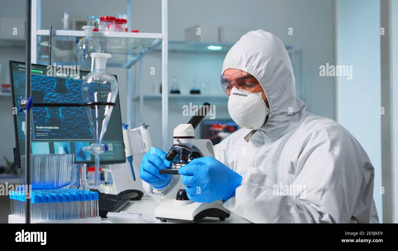 Scientist in ppe suit placing a slide on specimen stage of a laboratory ...
