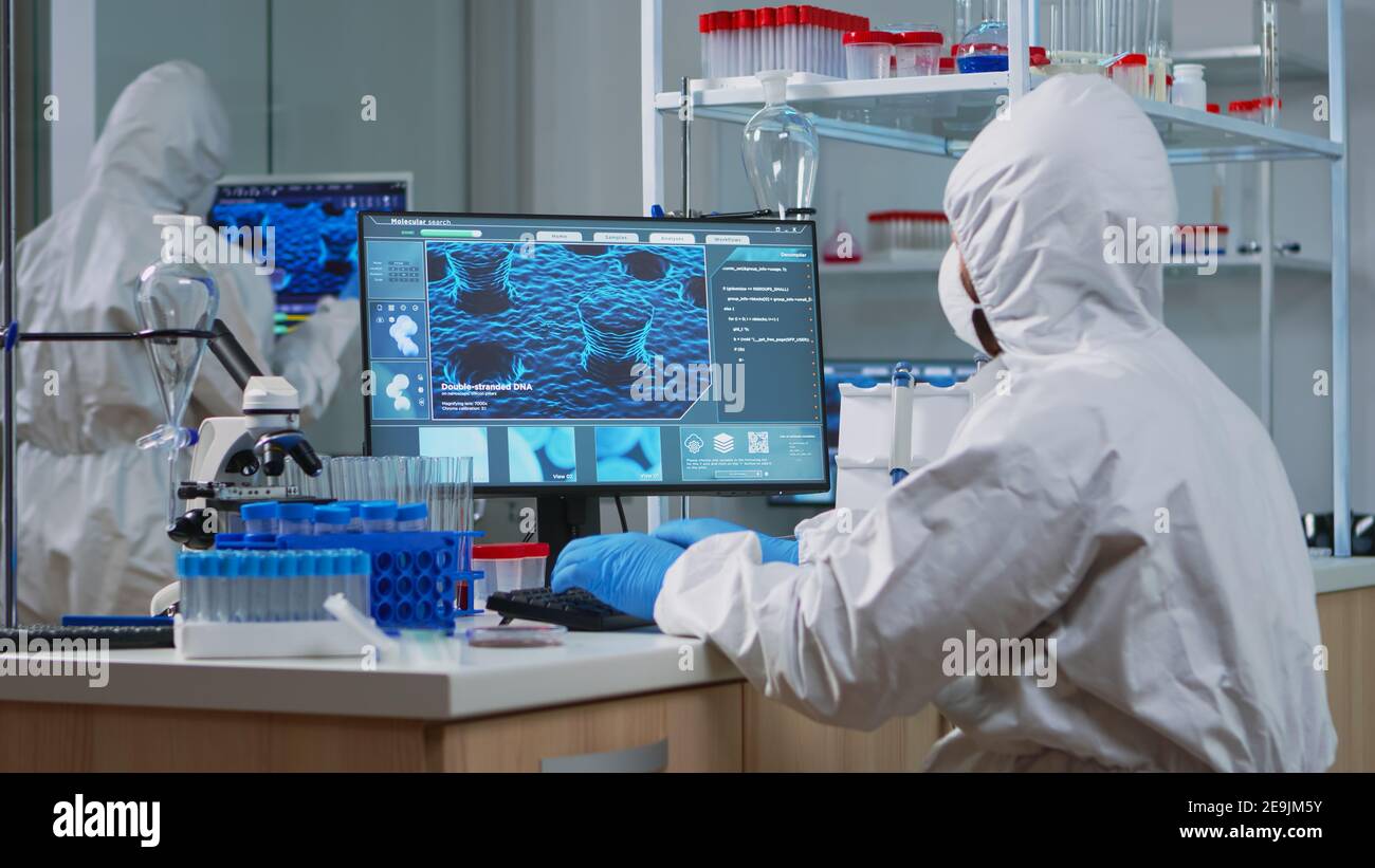 Medical scientist in ppe suit working with DNA scan image typing on pc ...