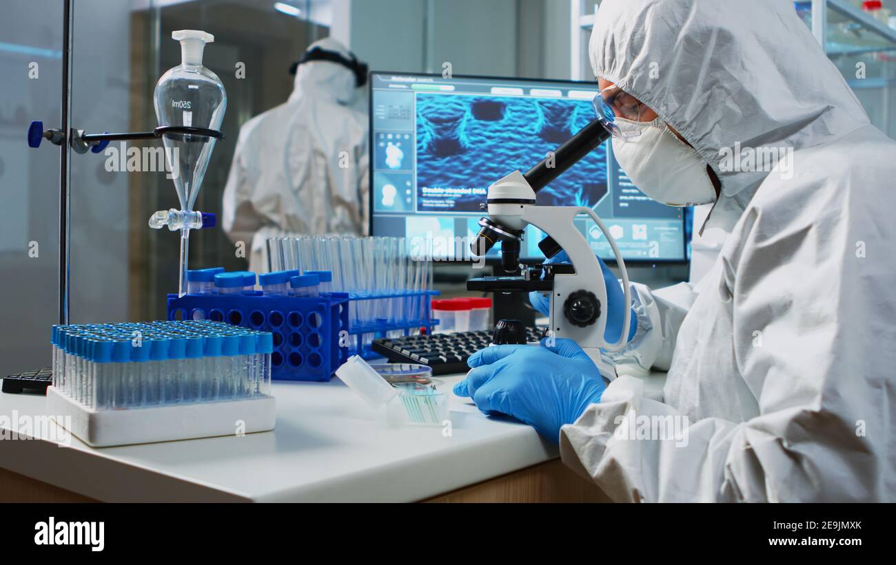 Scientist in protection suit looking through a microscope in equipped ...