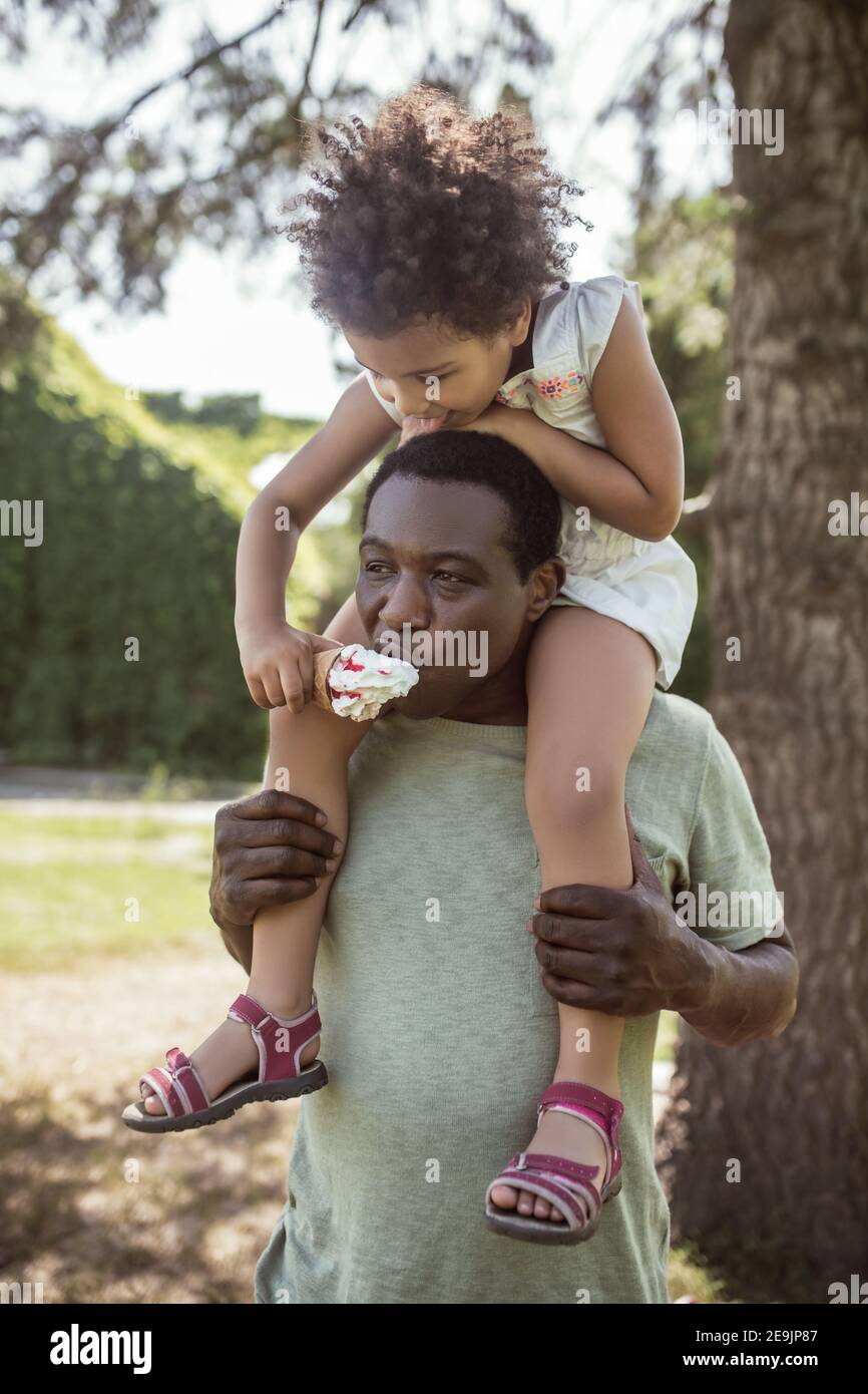 Dark-skinned cute kid sitting on her dads shoulders Stock Photo - Alamy