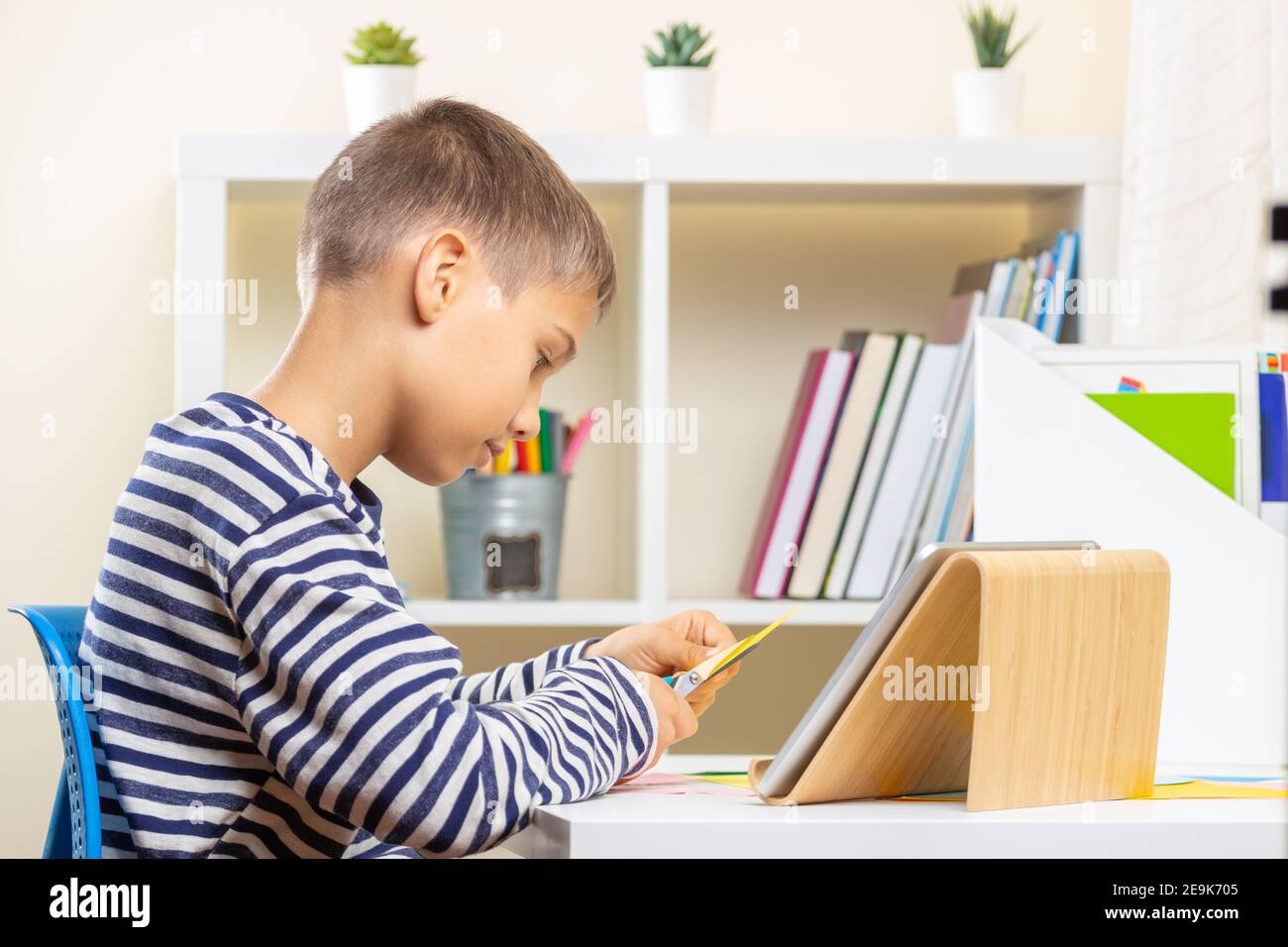 Boy cutting colored paper with scissors. Kid looking video tutorial and ...
